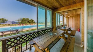 Um deck de madeira com mesas de piquenique, com vista para uma piscina e uma praia.