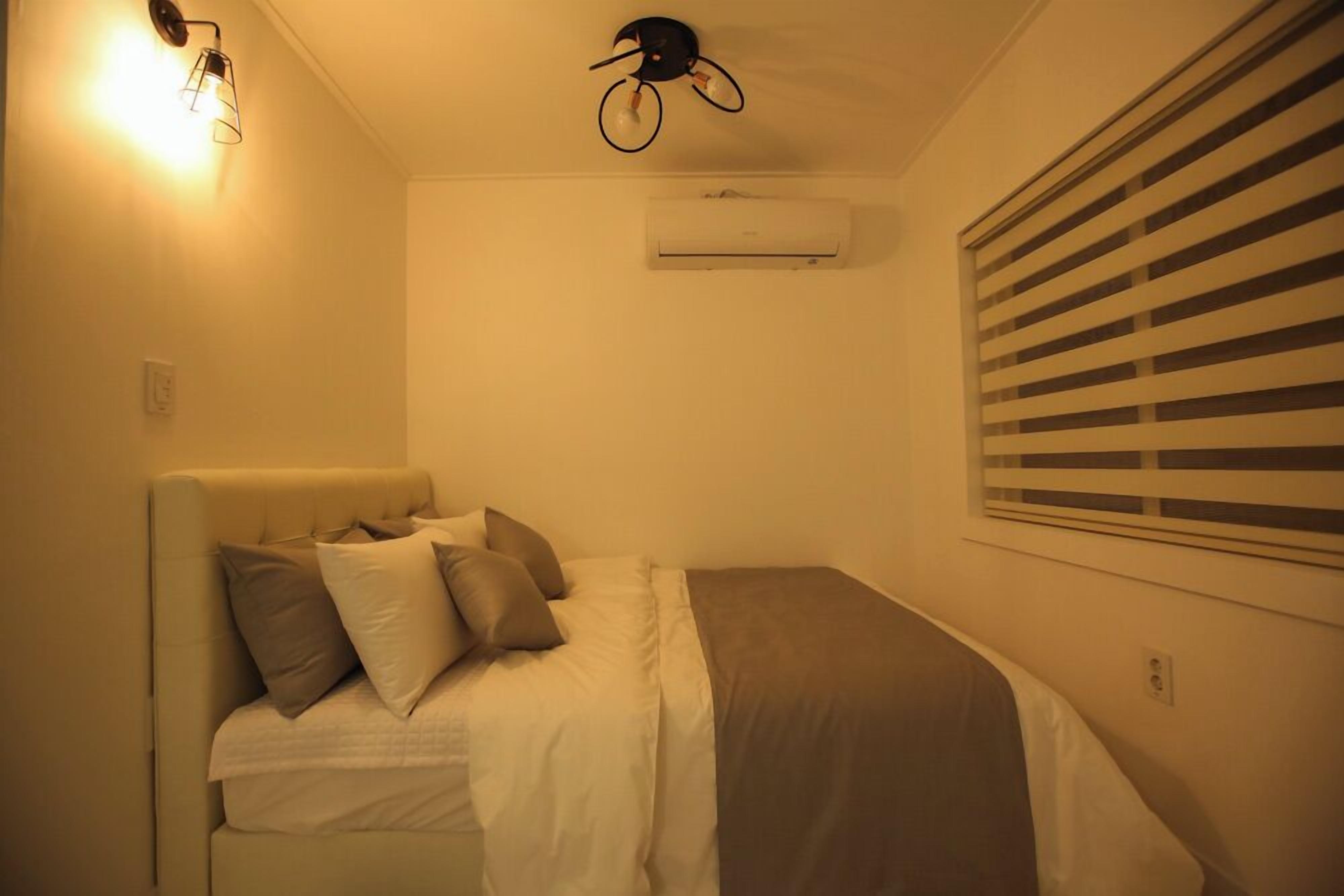 Quarto com cama, ar condicionado fixado na parede e luminária no teto.