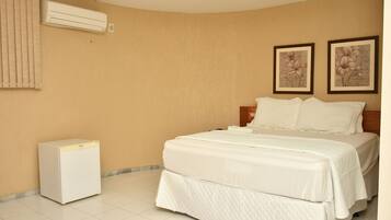 Quarto de hotel com uma cama, um pequeno frigorífico branco e duas imagens emolduradas com flores na parede.