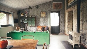 Quarto rústico com sofá verde, mesa de jantar de madeira e fogão antigo.