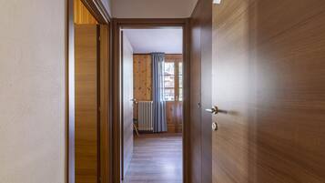 Um corredor com portas de madeira, um radiador e uma janela com cortinas.