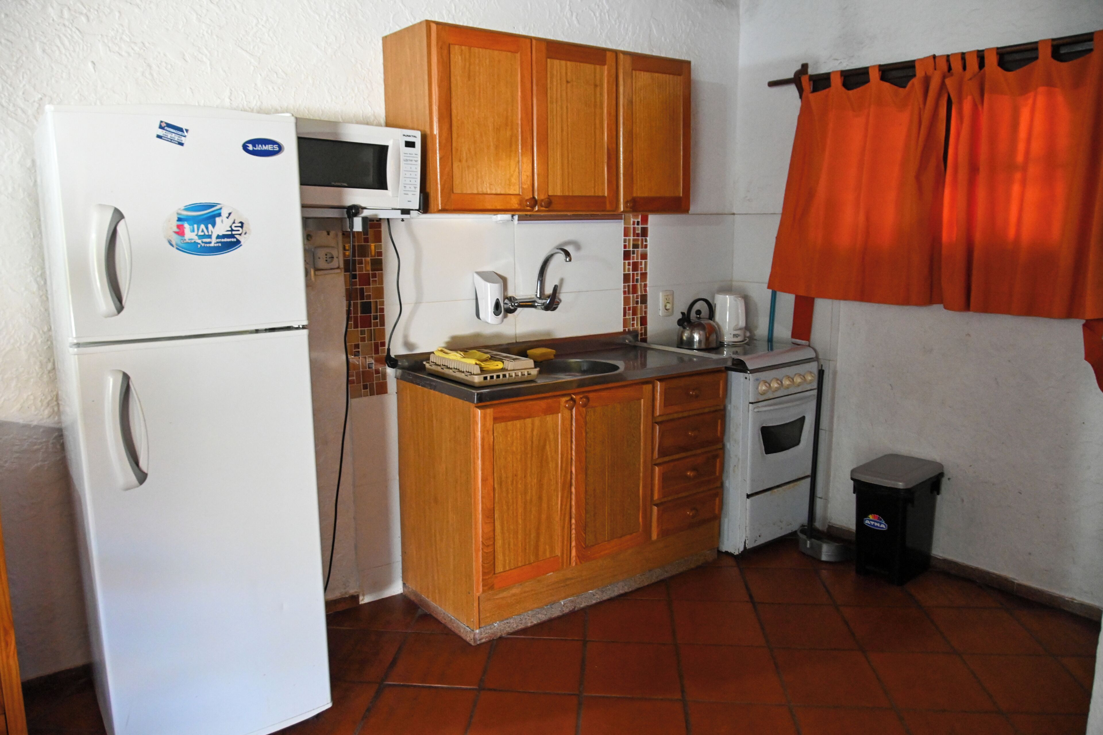 Cozinha compacta com armários de madeira, geladeira branca, micro-ondas, pia e forno.
