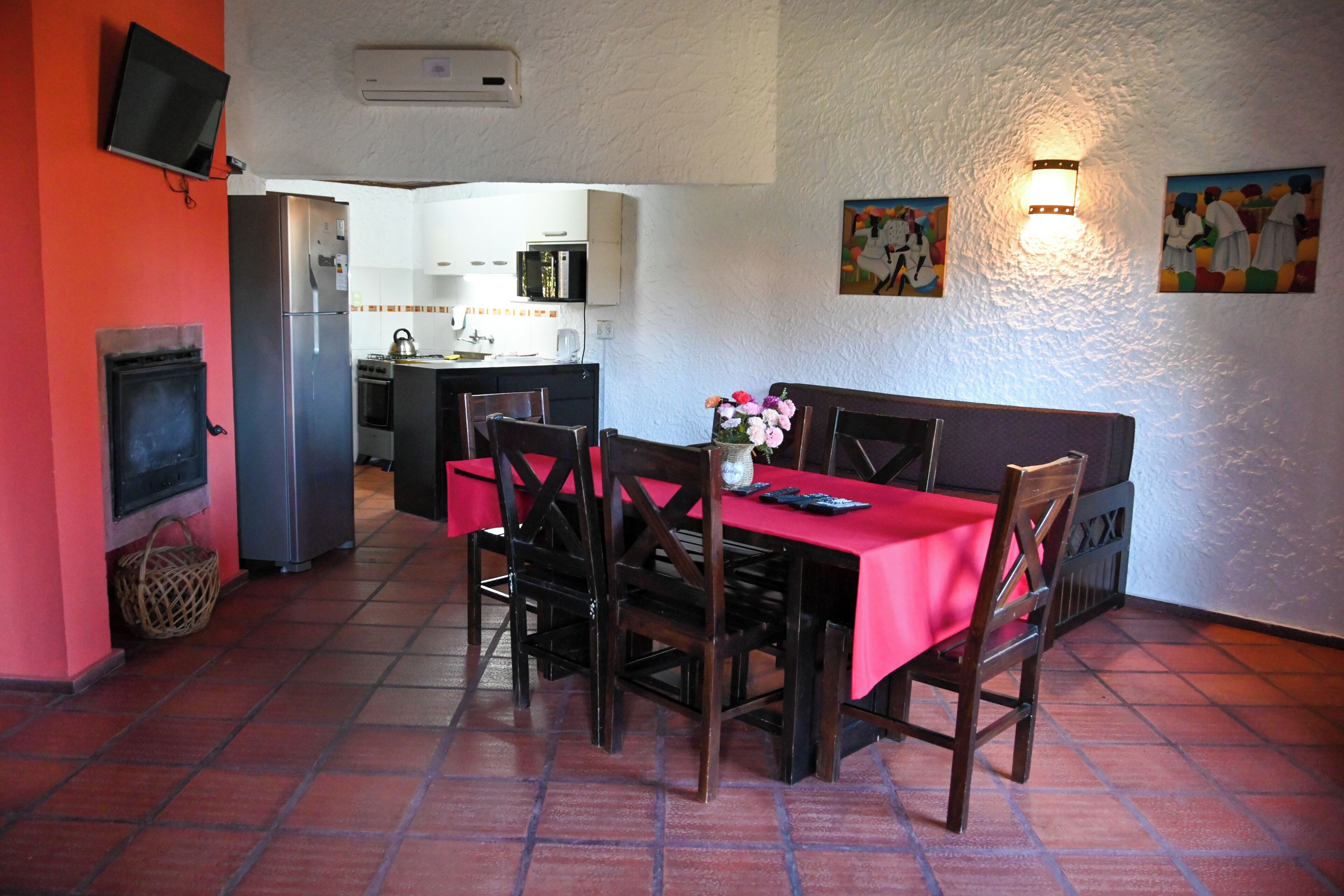 Uma sala de jantar com mesa e cadeiras vermelhas, cozinha ao fundo e obras de arte nas paredes.