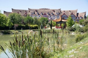 Um edifício tradicional com um grande lago à frente, rodeado por vegetação e um pavilhão.