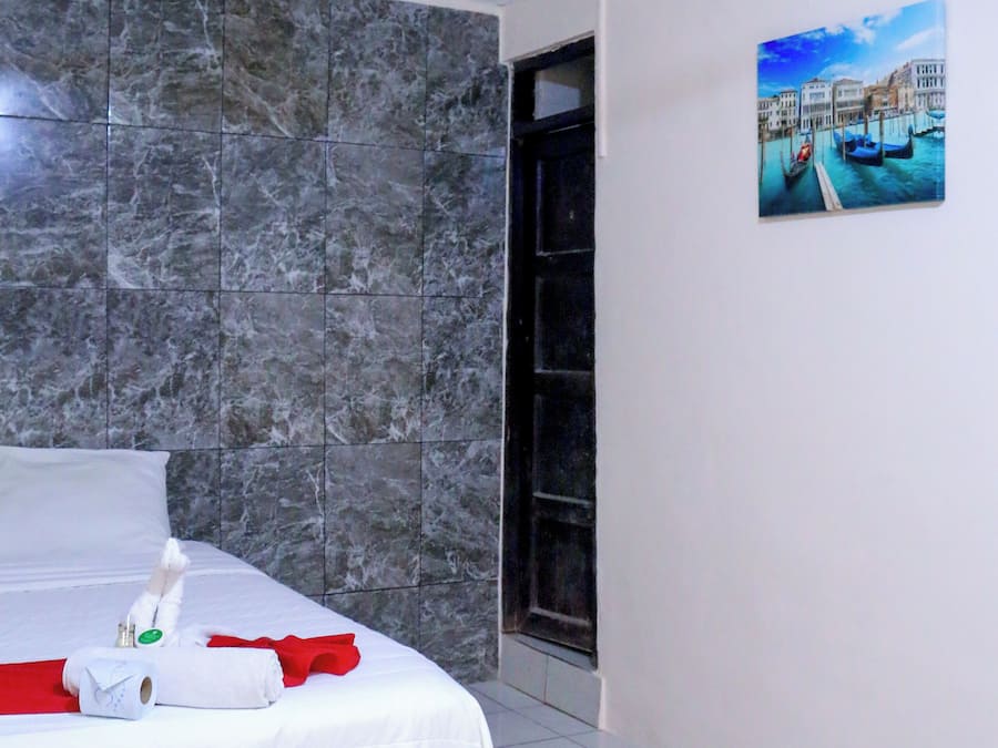 Quarto de hotel com cama, ventilador de teto, parede de mármore, porta e quadro de um canal.