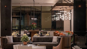 Uma sala de estar moderna com um sofá, uma mesa de centro e uma poltrona listrada. Ao fundo, há uma área de jantar com uma mesa e cadeiras.