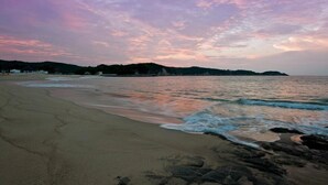 Uma praia com mar calmo, areal arenoso e colinas ao longe.