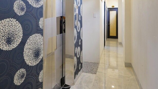 Corredor com parede estampada, divisória de vidro e piso ladrilhado que leva a uma porta.