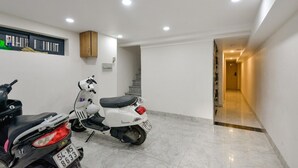 Corredor limpo e bem iluminado, com um scooter branco estacionado em primeiro plano e escada que leva a um andar superior.