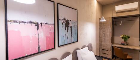Quarto de hotel moderno com cama, escrivaninha e duas grandes pinturas abstratas na parede.