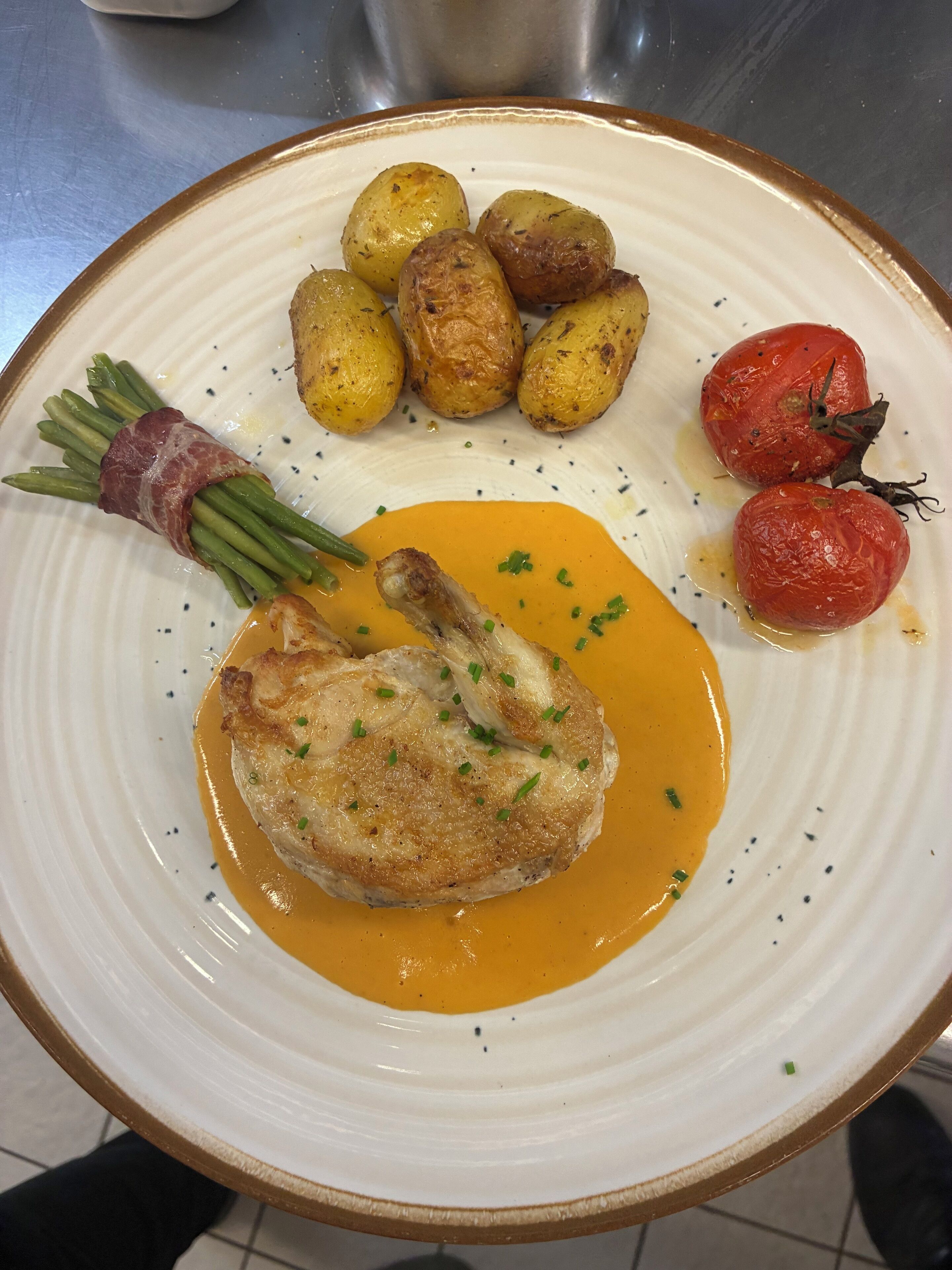 Um prato com batatas assadas, um tomate recheado e um pedaço de carne com molho.