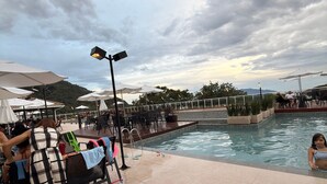 Uma área à beira da piscina com espreguiçadeiras e guarda-sóis, uma piscina e vista para a paisagem ao redor.