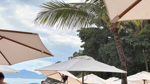 Um café à beira-mar com mesas ao ar livre, guarda-sóis e vista para o mar.