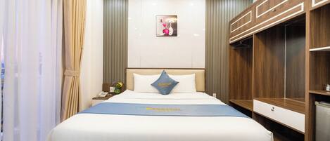 Quarto de hotel com cama, mesa de cabeceira, escrivaninha, guarda-roupa e um quadro na parede.