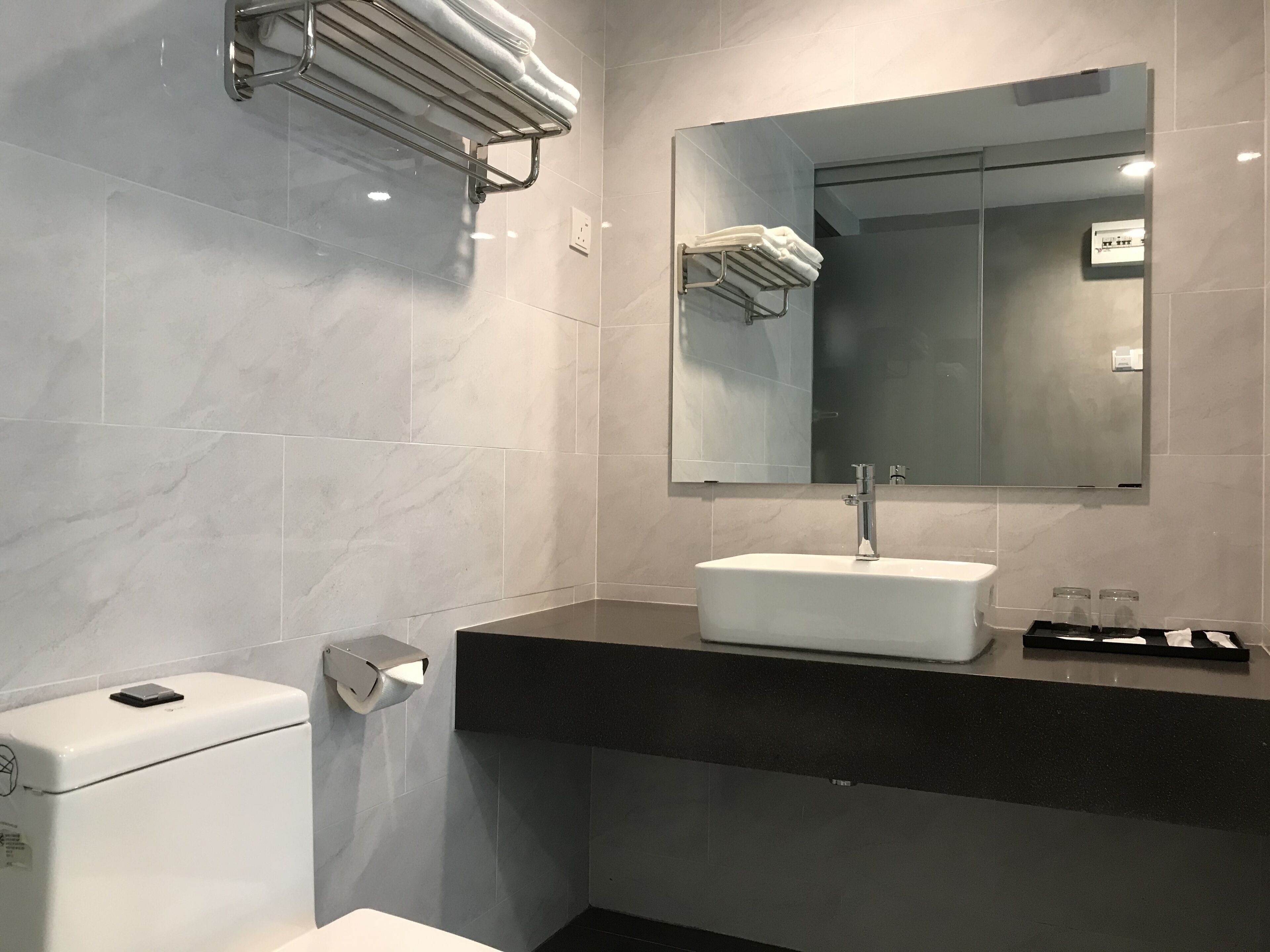 Uma casa de banho moderna com sanita branca, lavatório com bancada escura e espelho sobre o lavatório.
