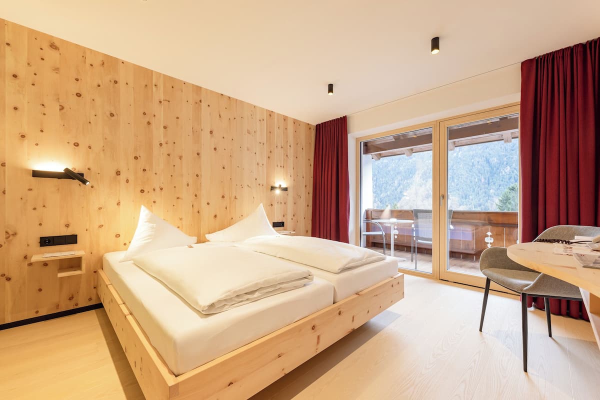 Quarto moderno com parede de madeira, uma cama grande, uma mesa de jantar e vista para uma paisagem nevada.