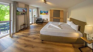 Quarto de hotel com uma cama grande, televisão na parede, uma mesinha e vista para o exterior.