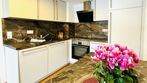 Uma cozinha moderna com armários brancos, bancada de mármore e forno embutido.
