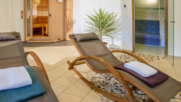 Uma área de spa com espreguiçadeiras de madeira, uma pequena planta em vaso e piso de azulejos.