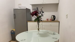 Uma cozinha compacta com geladeira, cafeteira e um vaso de flores sobre uma mesa de vidro.