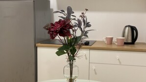 Uma cozinha com geladeira branca, bancada de madeira e um vaso de flores sobre uma mesa de vidro.