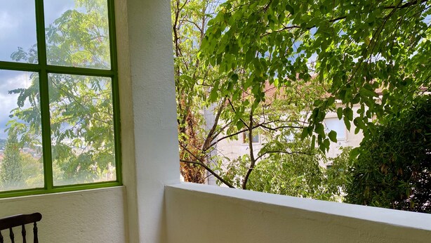Quarto com uma janela grande, uma mesa redonda e uma cadeira de madeira.
