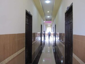 Um corredor com piso espelhado, portas em ambos os lados e uma pessoa caminhando em direção ao final.
