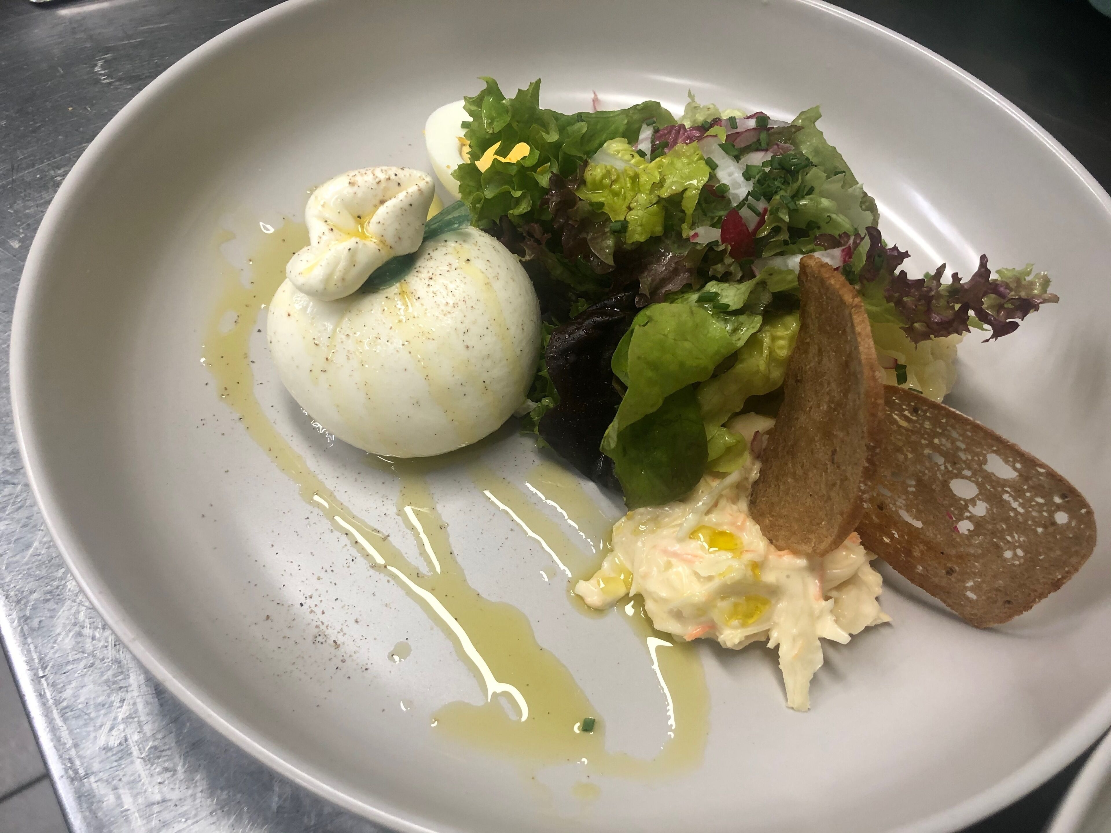 Um prato branco com salada, ovo pochê e uma fatia de pão.