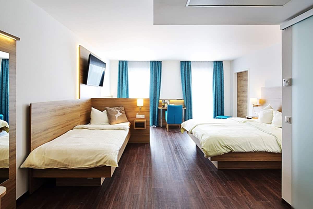 Quarto de hotel com duas camas, uma escrivaninha e uma televisão fixada na parede.