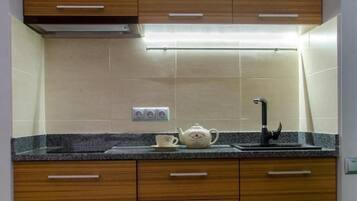 Uma cozinha compacta com armários de madeira, bancada de granito, chaleira e uma torneira moderna.