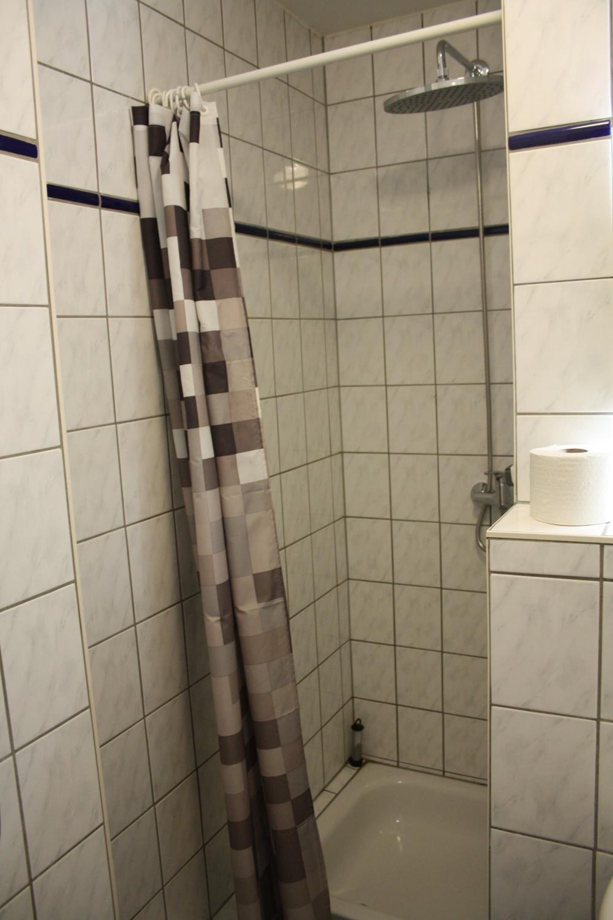 Um chuveiro com cortina quadriculada, paredes revestidas de azulejos e um chuveiro manual.