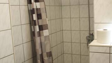 Um chuveiro com cortina quadriculada, paredes revestidas de azulejos e um chuveiro manual.