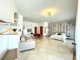 Quarto de hotel moderno com sofá, cama, área de jantar e cozinha.