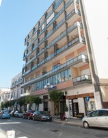 Edifício com vários andares, varandas, área de estacionamento e vista para a rua.