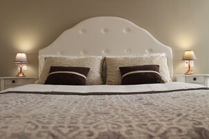 Cama bem arrumada com colcha estampada e duas almofadas decorativas, com duas mesas de cabeceira com abajures de cada lado.