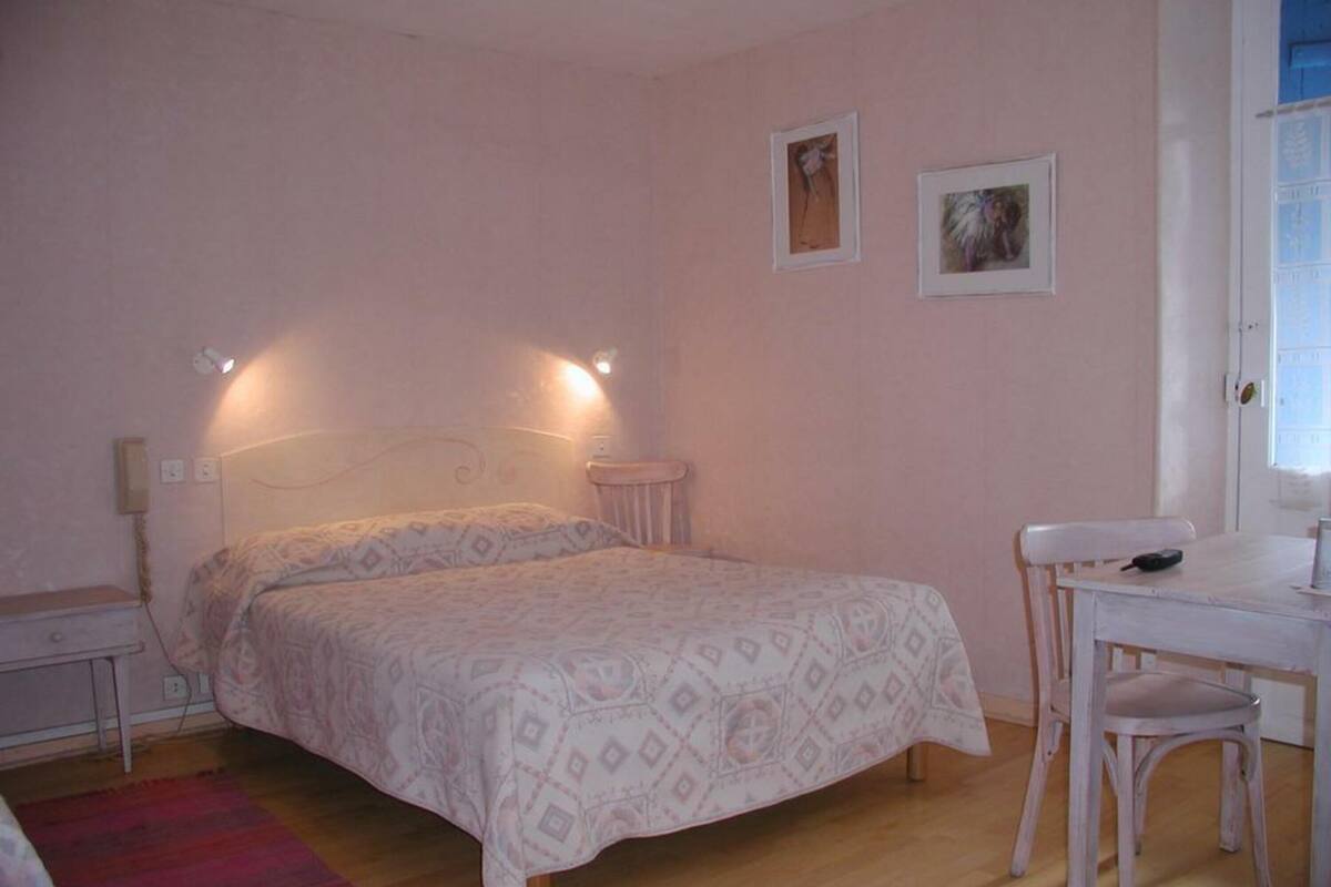 Quarto com cama, mesa de cabeceira, cadeira e escrivaninha com cadeira. Há duas imagens emolduradas na parede.