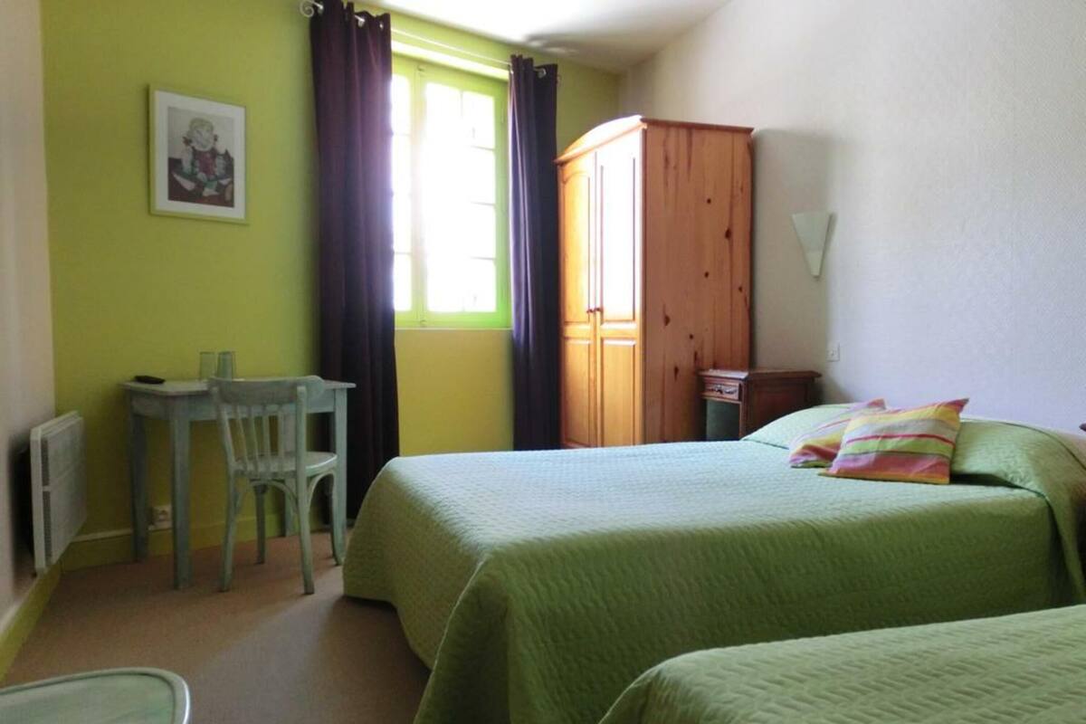Quarto com duas camas, uma escrivaninha, uma cadeira, um guarda-roupa e um radiador.