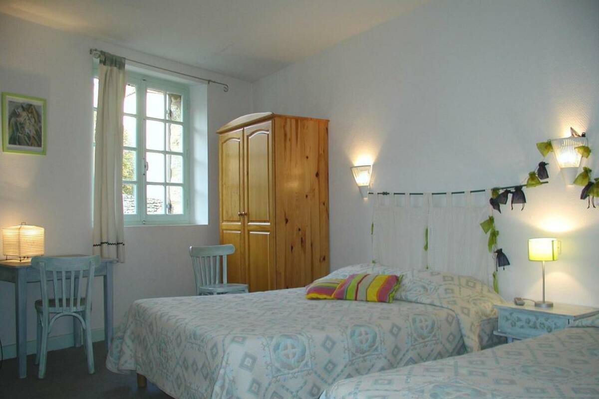 Quarto com duas camas, guarda-roupa de madeira, escrivaninha com cadeira e janela com cortinas.