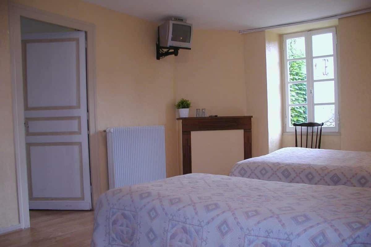 Quarto com duas camas, um radiador, uma mesinha com uma planta e uma janela com vista para o verde.