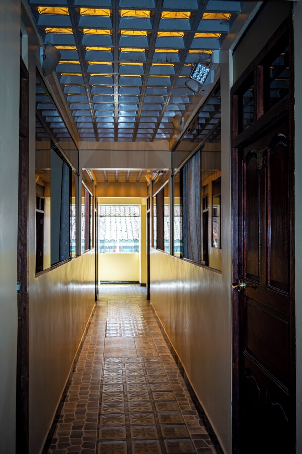 Um corredor com piso estampado, uma porta de madeira à direita e uma janela no final.
