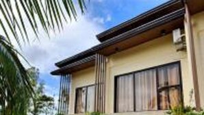 Uma casa moderna de dois andares com telhado plano, janelas amplas e um jardim bem cuidado com degraus que levam à entrada.
