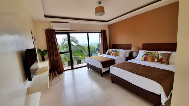 Quarto de hotel com duas camas, televisão, janela grande com cortinas e ventoinha no teto.