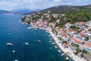 Uma vila costeira com um porto, casas com telhados vermelhos e montanhas ao fundo.