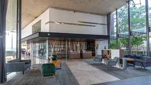 Um lobby de hotel moderno com balcão de recepção, área de estar e grandes janelas com vista para o exterior.