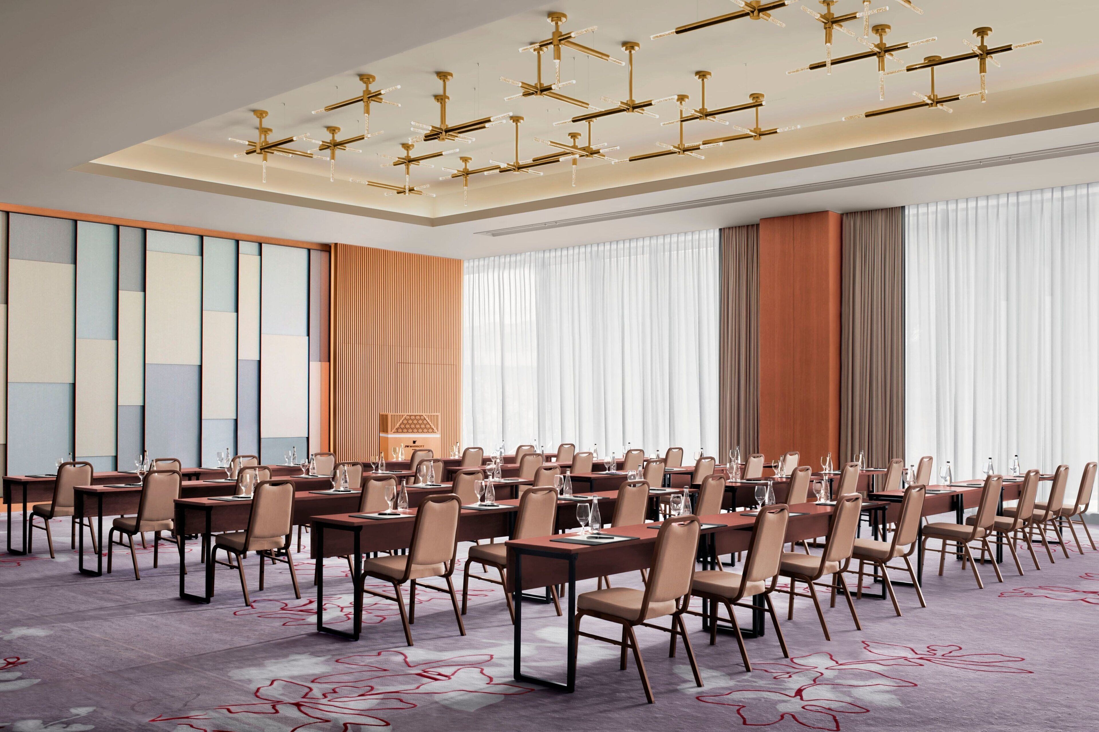 Sala de conferência com várias mesas e cadeiras, carpete estampado e um lustre moderno.