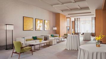 Um hall amplo com design moderno, com um sofá, poltronas, uma mesa de centro e uma mesa redonda com um vaso de flores.