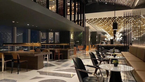 Interior moderno com área de bar, assentos e vista da cidade à noite.
