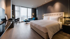 Quarto de hotel moderno com uma cama grande, uma mesa, uma cadeira e vista para a cidade.