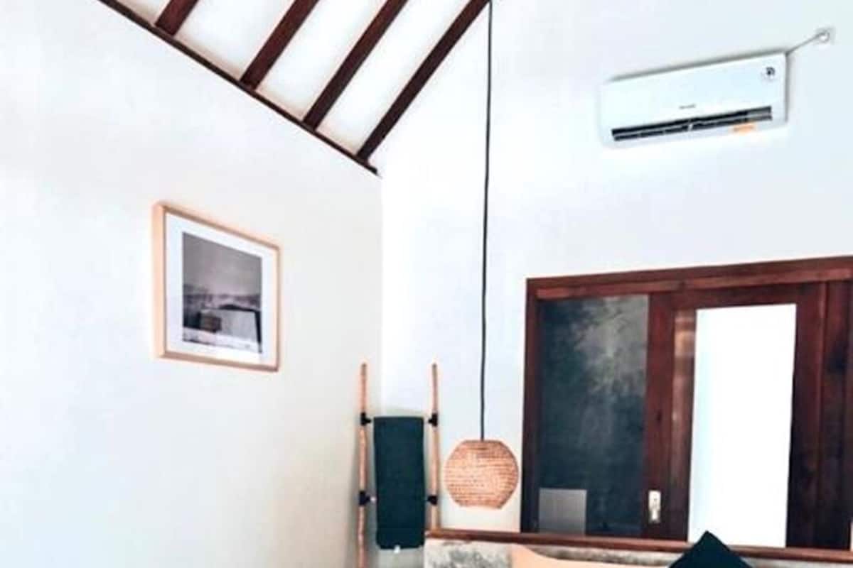 Quarto com cama, ar condicionado na parede, quadro emoldurado e luminária pendente.