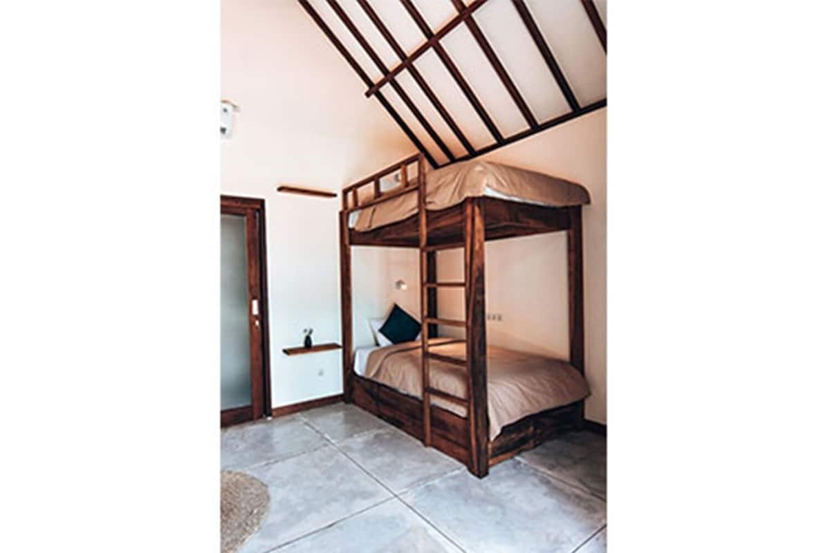Quarto com beliche de madeira, uma pequena prateleira e uma porta.